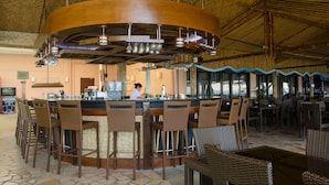Uma área de bar com balcão curvo, cadeiras de vime e uma pessoa trabalhando atrás do balcão.