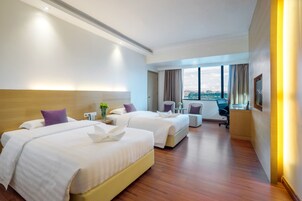 Quarto de hotel com duas camas, uma escrivaninha, uma cadeira e uma janela grande com vista para a cidade.