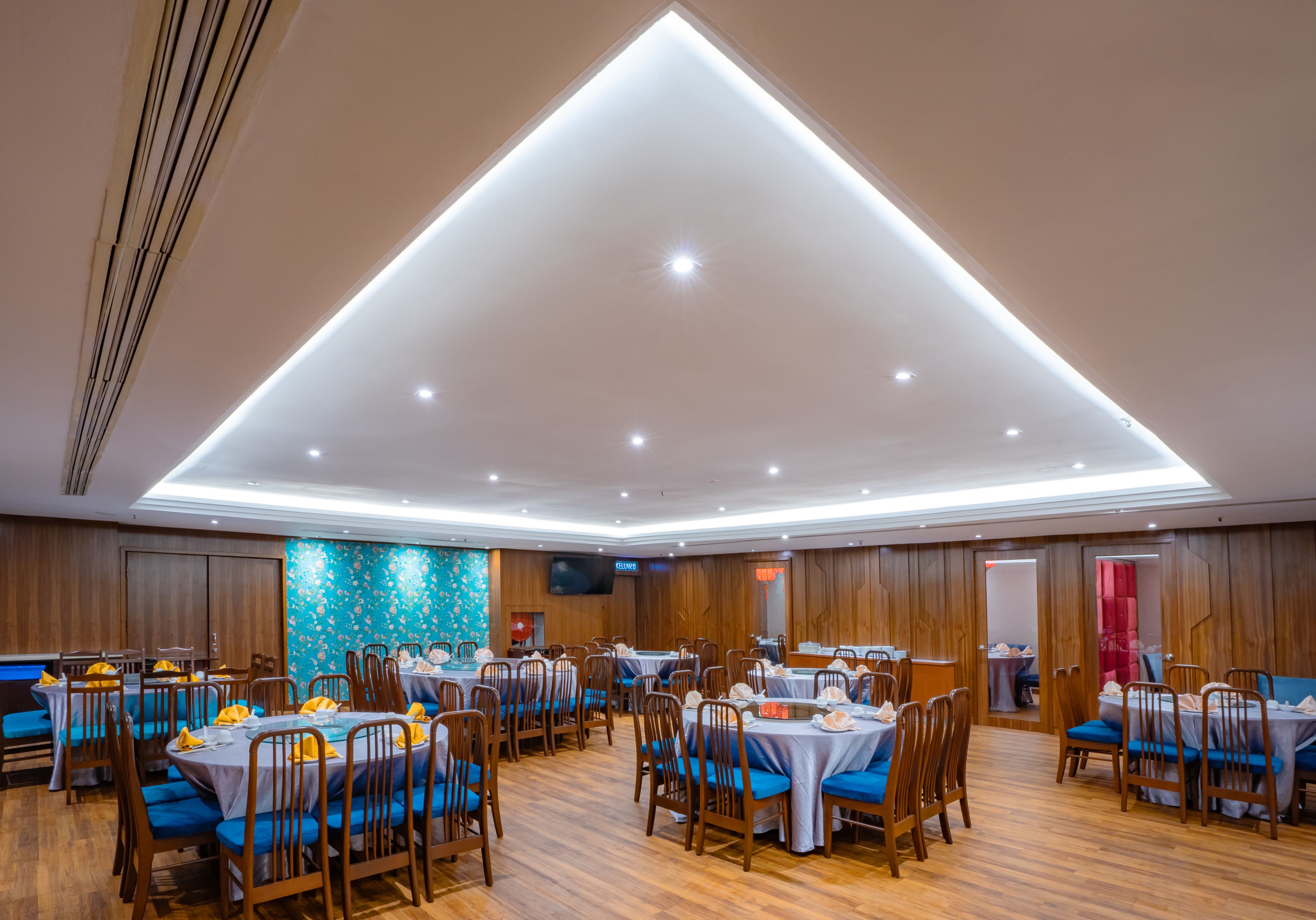 Uma sala de jantar espaçosa com várias mesas e cadeiras, painéis de madeira nas paredes e um design de teto moderno.