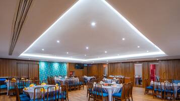 Uma sala de jantar espaçosa com várias mesas e cadeiras, painéis de madeira nas paredes e um design de teto moderno.
