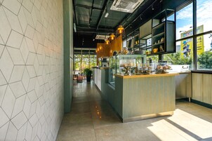 Um café moderno com interior decorado com azulejos, um balcão central com produtos de pastelaria e amplas janelas com vista para o exterior.
