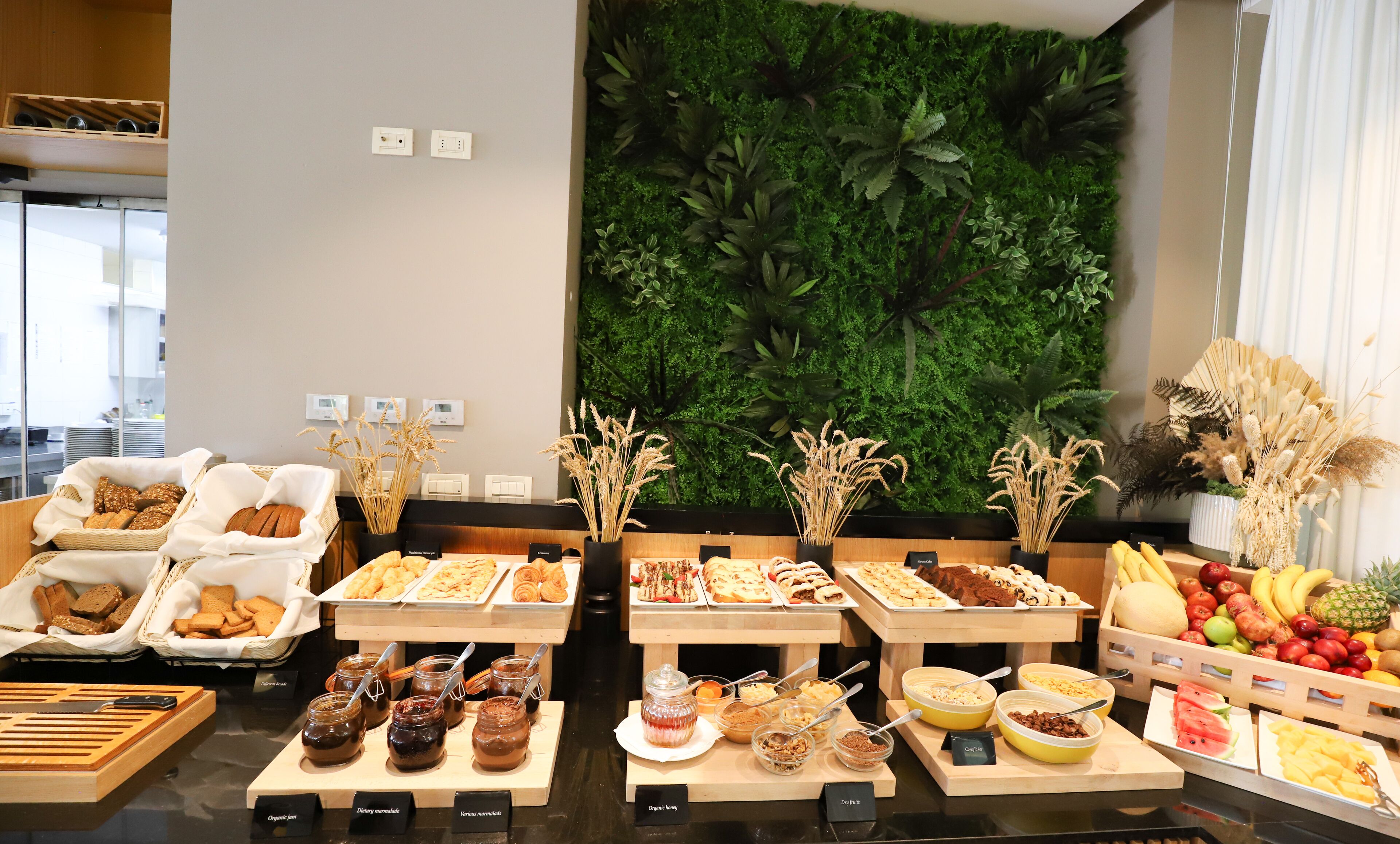 Buffet com diversas opções de comida, parede com jardim vertical e janela com cortinas.