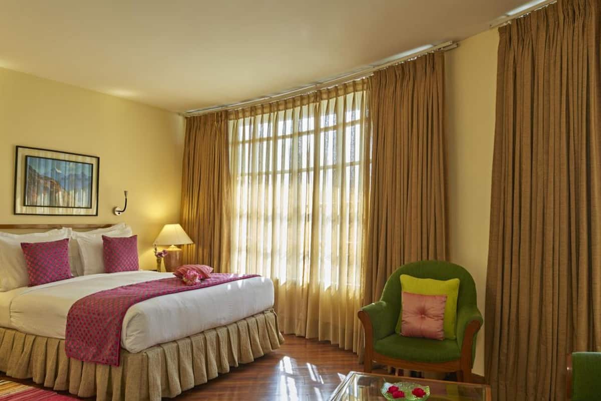Quarto de hotel com cama, cadeira, mesa e cortinas.