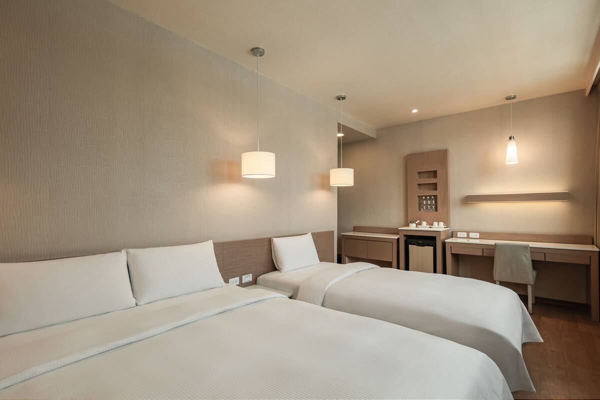 Quarto de hotel com duas camas, uma escrivaninha e uma cadeira.