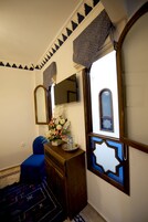 Um quarto com um armário de madeira, um espelho, uma cadeira azul e uma parede decorativa com padrões geométricos.