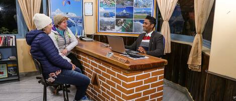 Balcão de informações turísticas com um laptop, bancada de madeira e um mural com fotos de viagens.