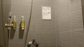 Área de chuveiro com azulejos cinzas, chuveiro manual, secador de mãos e dosador de sabonete.