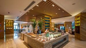 Um lobby de hotel moderno com área de buffet central, painéis de madeira no teto e piso limpo e lustroso.