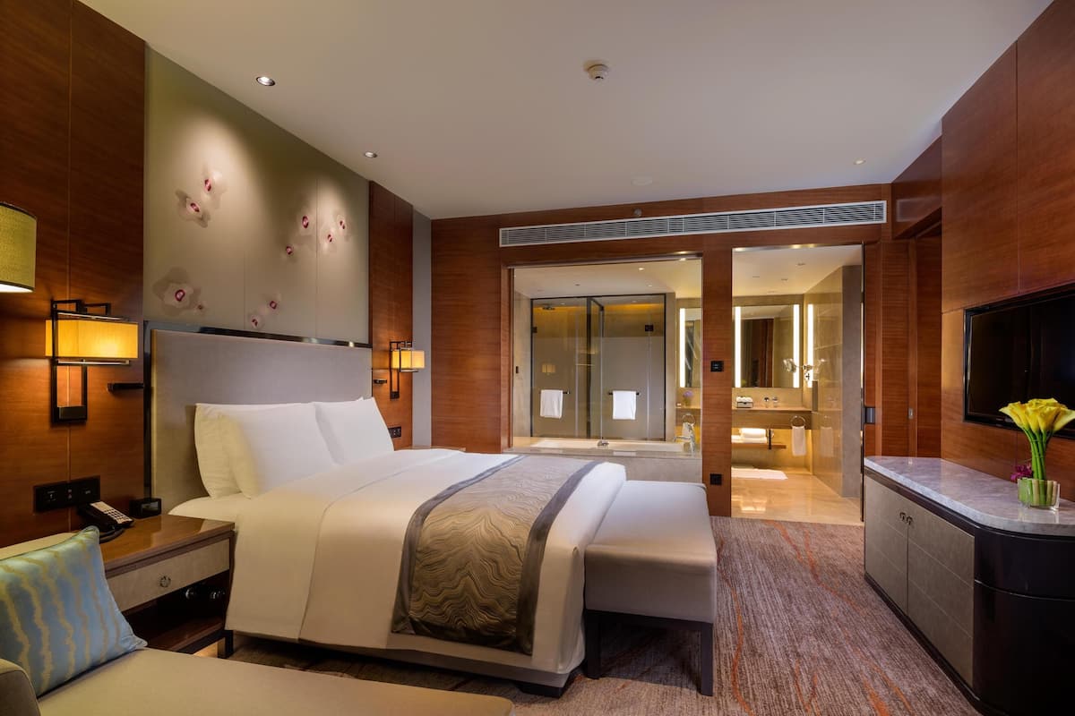 Quarto de hotel com cama, mesa de cabeceira, abajur e vista para o banheiro.