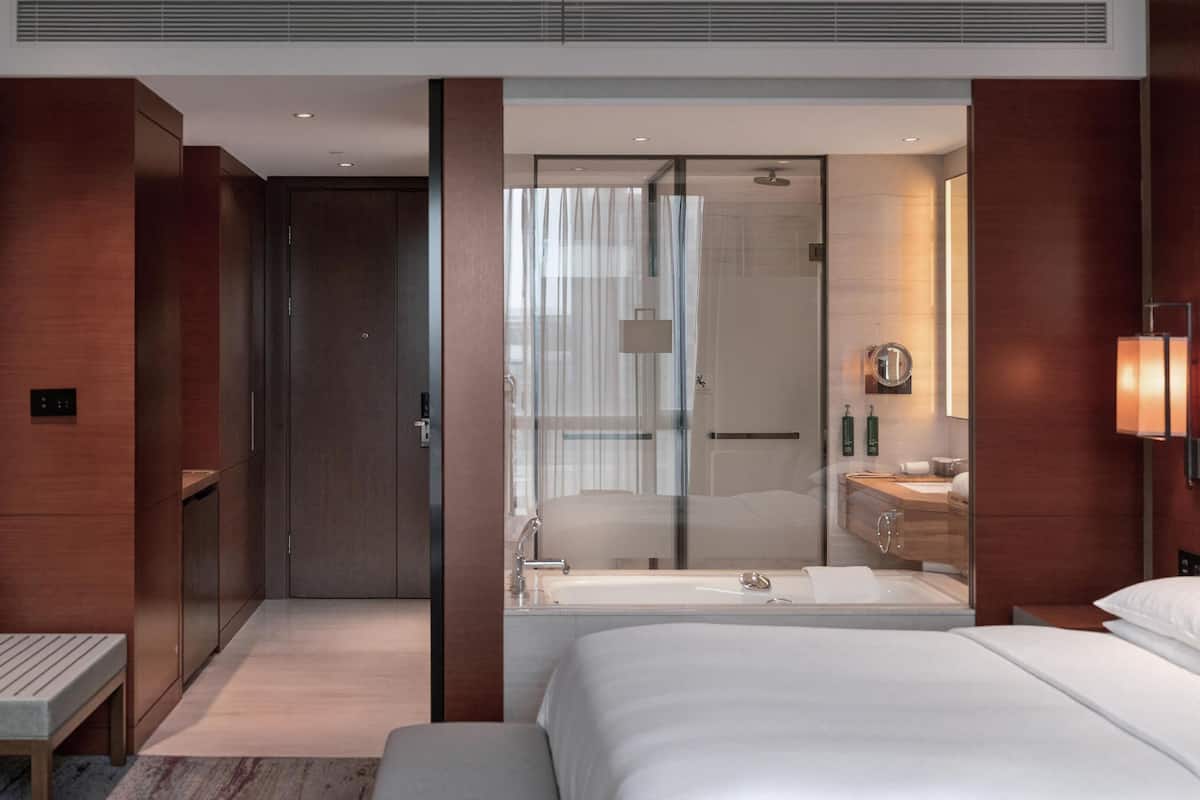 Quarto de hotel moderno com uma cama grande, área de chuveiro separada e closet espaçoso.