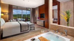 Quarto de hotel moderno com uma cama grande, um espaço de estar, banheiro com banheira e vista para o exterior.