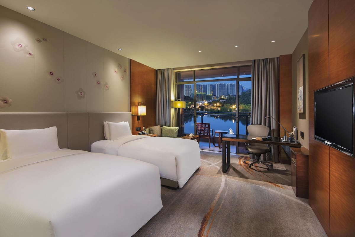 Quarto de hotel com duas camas, uma mesa, uma cadeira, uma TV e vista para a cidade.