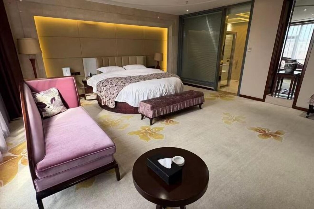 Quarto de hotel com cama, sofá, banco e uma pequena mesa.