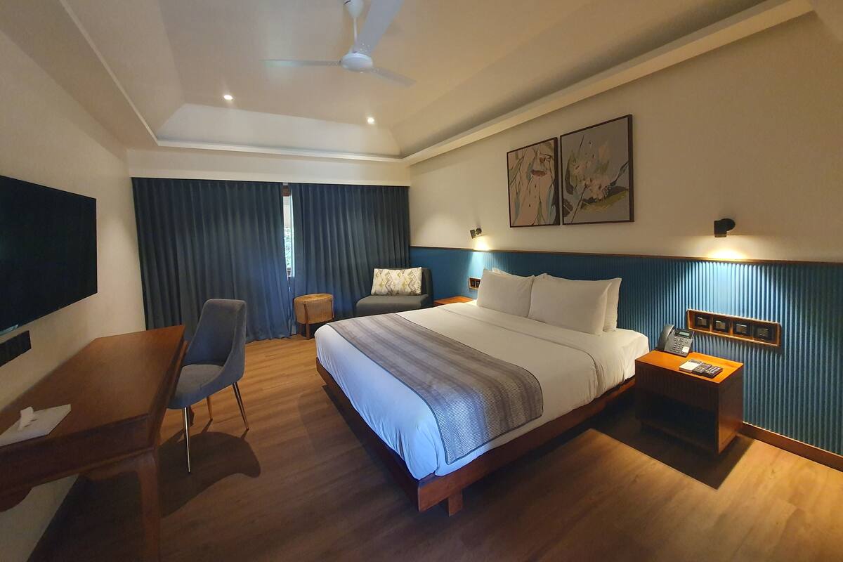 Quarto de hotel com uma cama grande, uma escrivaninha, uma cadeira, mesa de cabeceira com telefone e ventoinha no teto.