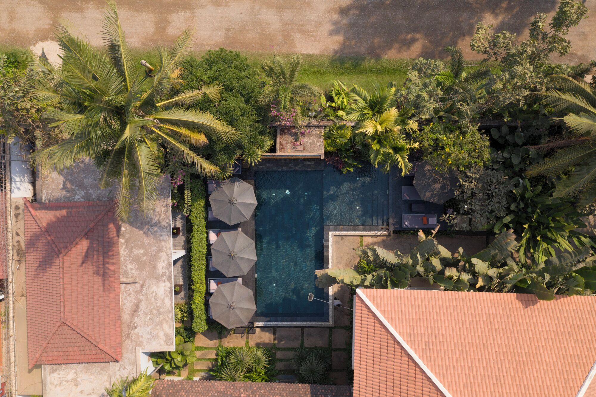 Vista aérea de uma área residencial com piscina, vegetação tropical e um edifício com telhado vermelho.