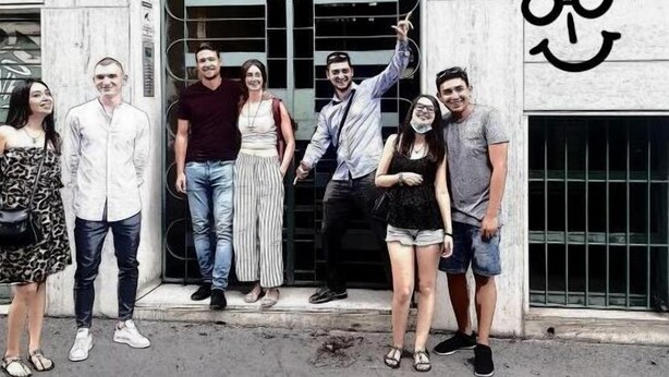 Um grupo de pessoas em frente a um edifício com o número 35 na porta e uma carinha sorridente de óculos e um sinal de mais na parede.