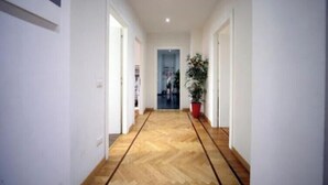 Um corredor com piso de madeira, paredes brancas e um vaso com planta.