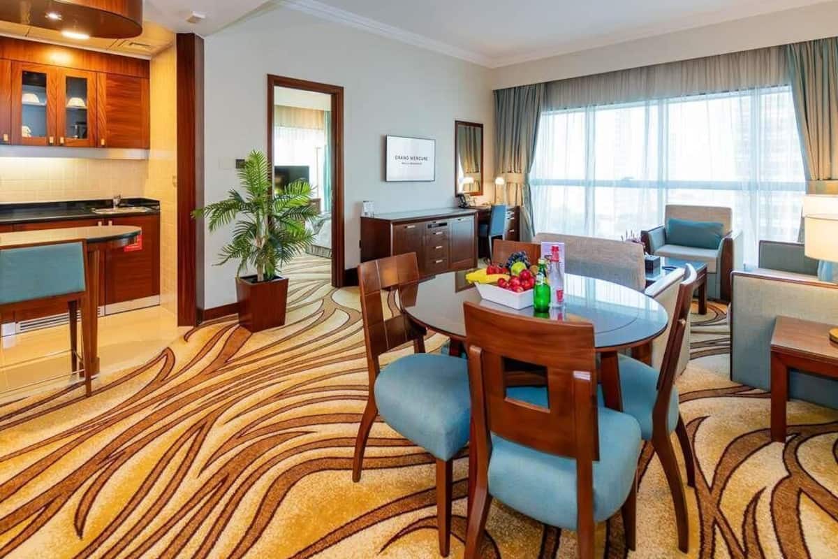 Quarto de hotel com área de jantar, cozinha, janela grande e planta em vaso.