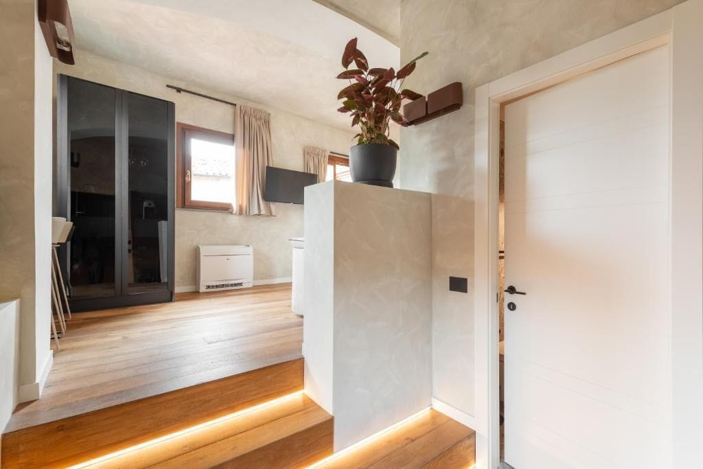 Interior moderno com piso de madeira, porta branca e uma planta em vaso sobre um pedestal branco.