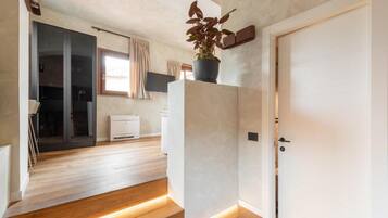 Interior moderno com piso de madeira, porta branca e uma planta em vaso sobre um pedestal branco.