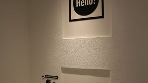 Um corredor com uma placa que diz "Hello!", uma escada com corrimão e um acessório de iluminação fixado na parede.