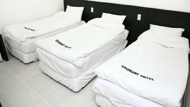 Três camas de solteiro com roupa de cama e almofadas brancas, cada uma identificada como 'Economy Hotel'.