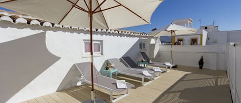 Terraço no telhado com espreguiçadeiras, um grande guarda-sol e uma pequena mesa com uma planta.