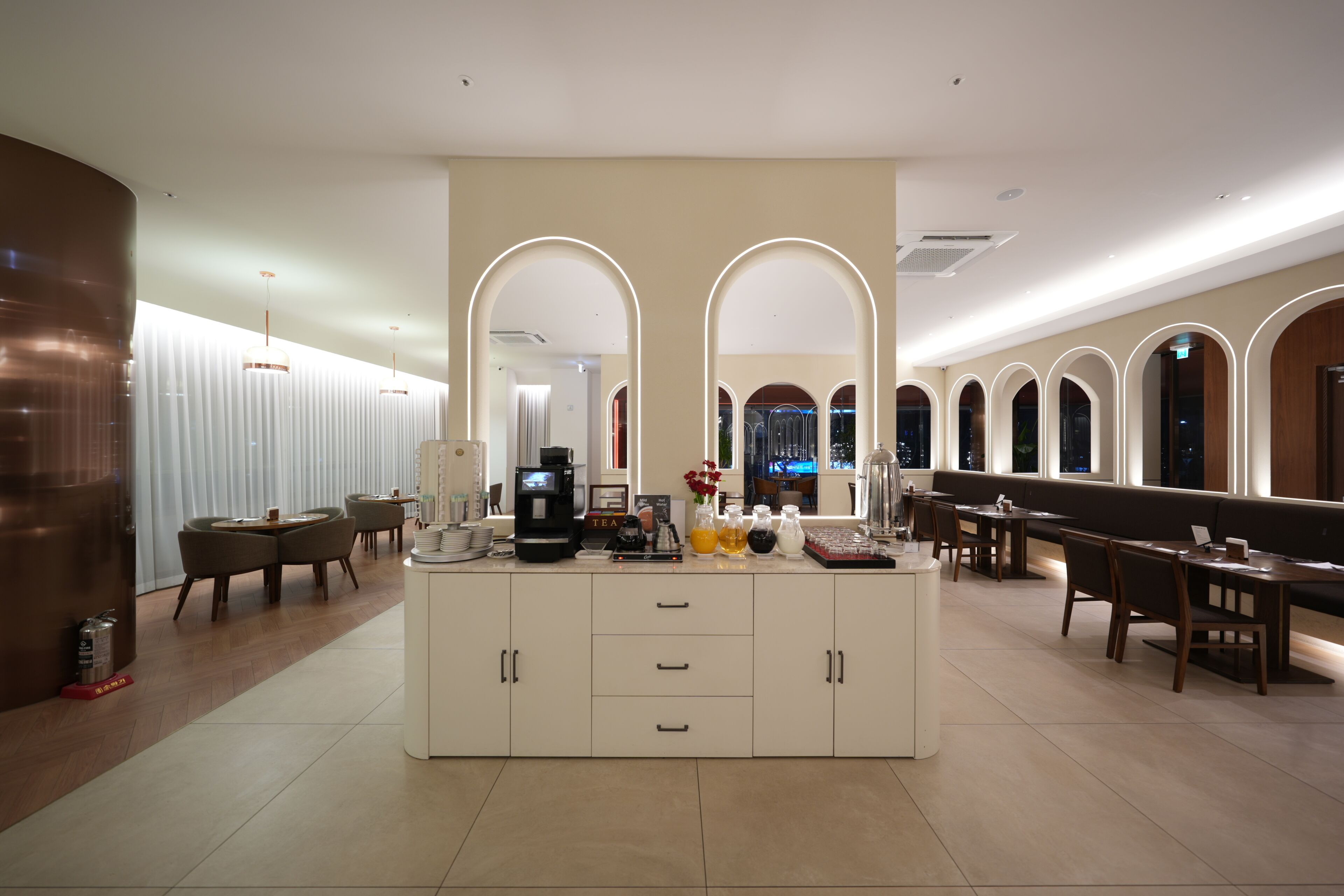 Um hall de hotel moderno com ilha central, área de estar e janelas em arco.