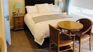 Quarto de hotel com cama, mesa de cabeceira, luminária, cadeira e vista para o exterior.