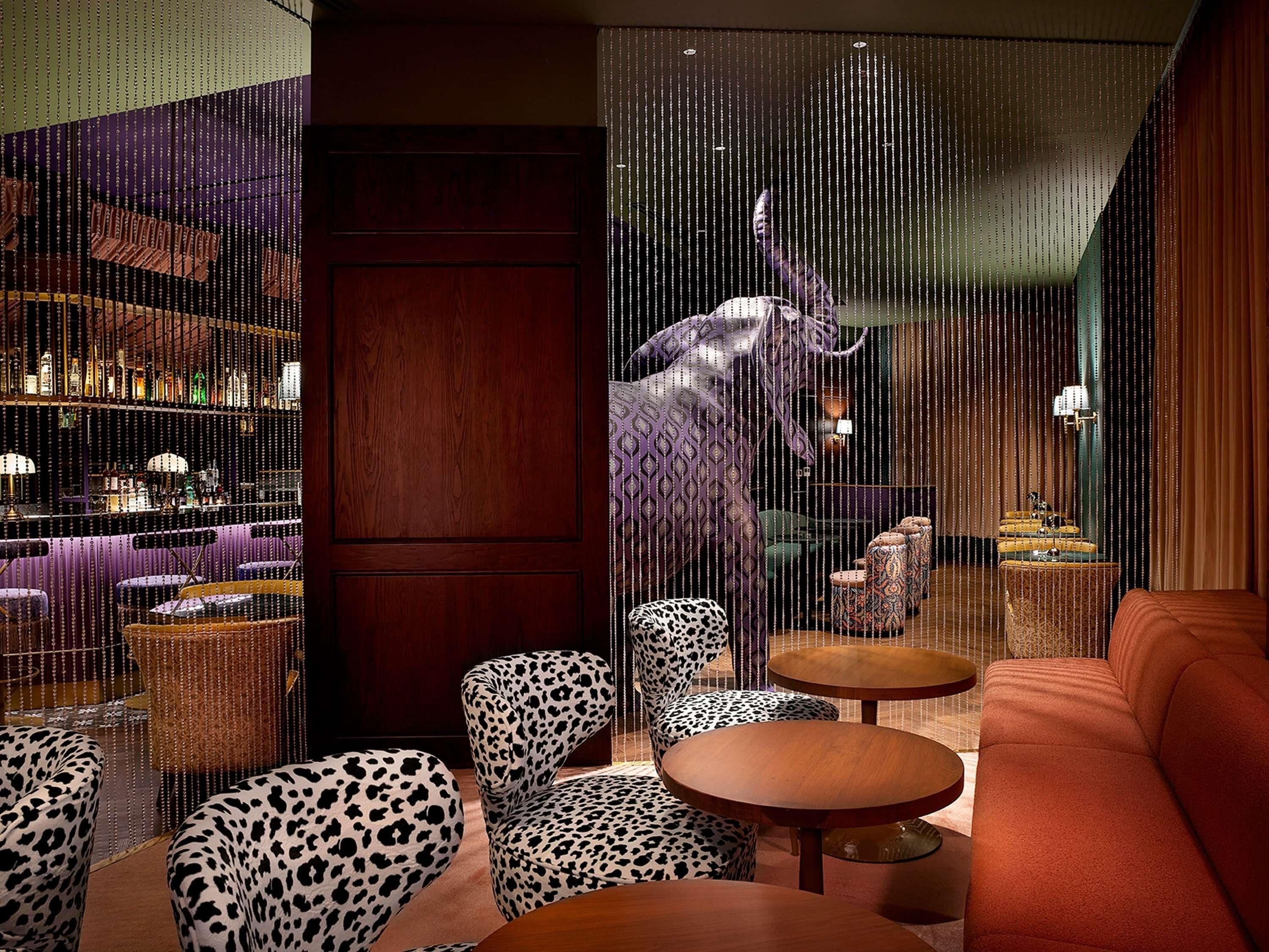 Uma área de bar com diversas opções de assento, incluindo cadeiras com estampa de leopardo e um sofá, um dossel estampado e um balcão repleto de garrafas.