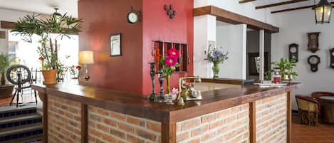 Um saguão de hotel com uma mesa de recepção de tijolos, um relógio e diversos vasos de plantas.