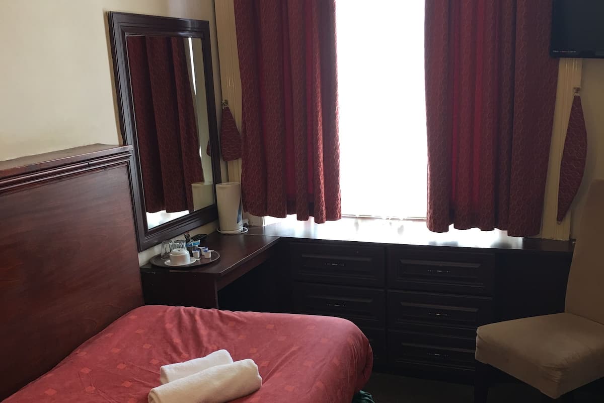Quarto de hotel com uma cama grande, cômoda, espelho, cadeira e janela com cortinas.