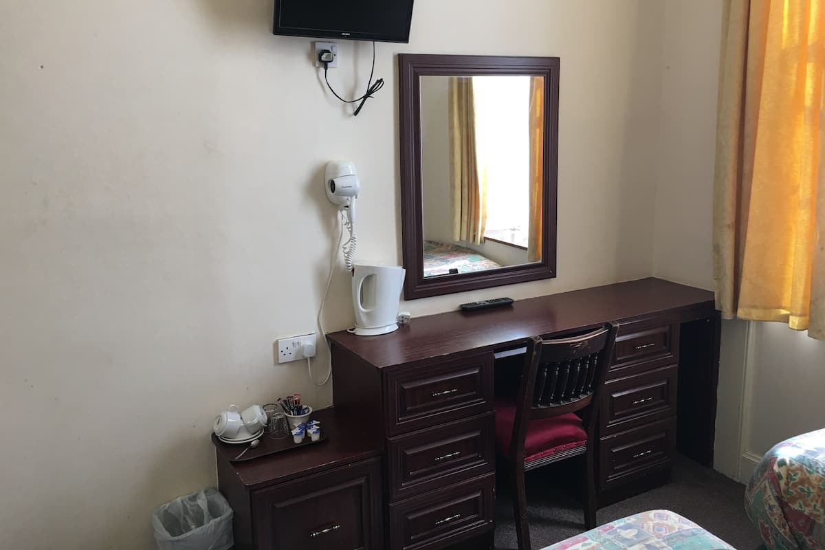 Quarto de hotel com penteadeira de madeira, espelho, secador de cabelo, máquina de café e televisão presa à parede.