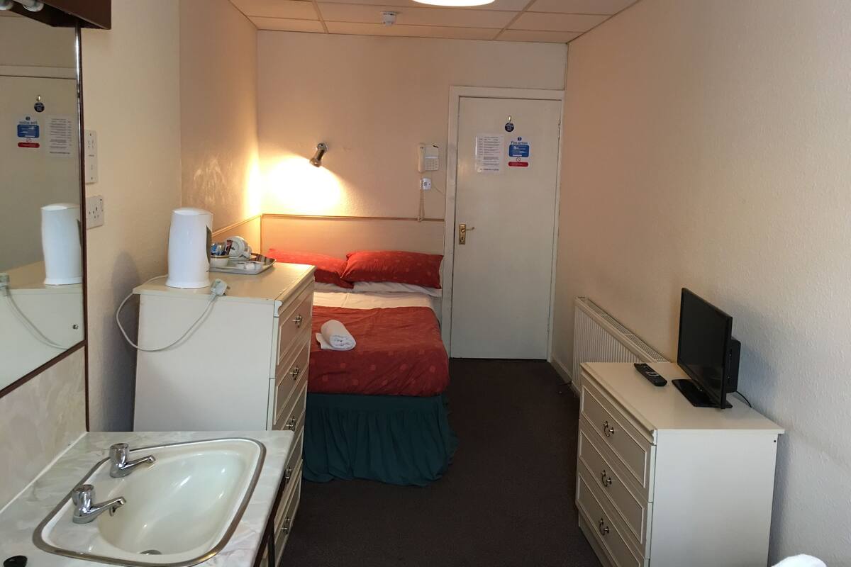 Quarto de hotel com uma cama, uma escrivaninha com computador, pia e espelho.