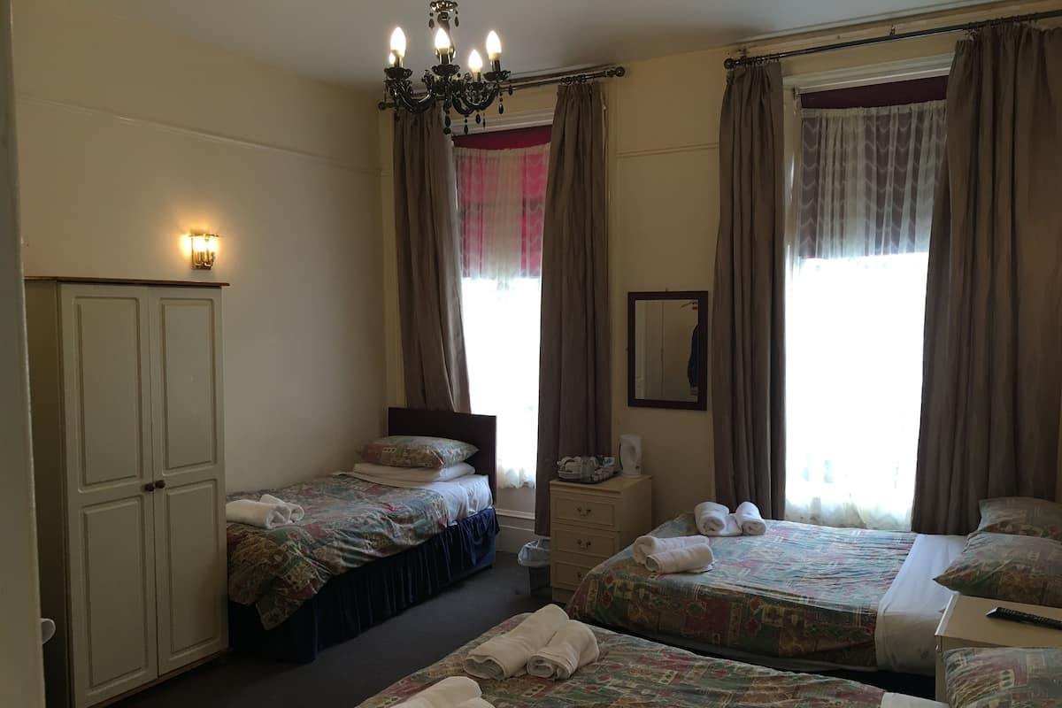 Quarto de hotel com duas camas, um guarda-roupa, um candelabro, um espelho e uma janela com cortinas.