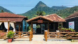 Entrada de hotel com montanhas ao fundo, com telhado de azulejos, cerca de madeira e uma placa.