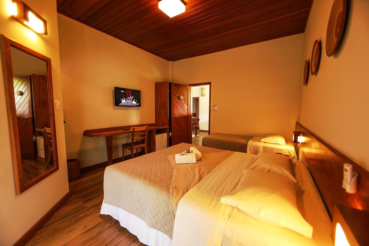 Quarto de hotel com duas camas, uma escrivaninha, uma cadeira e uma televisão.
