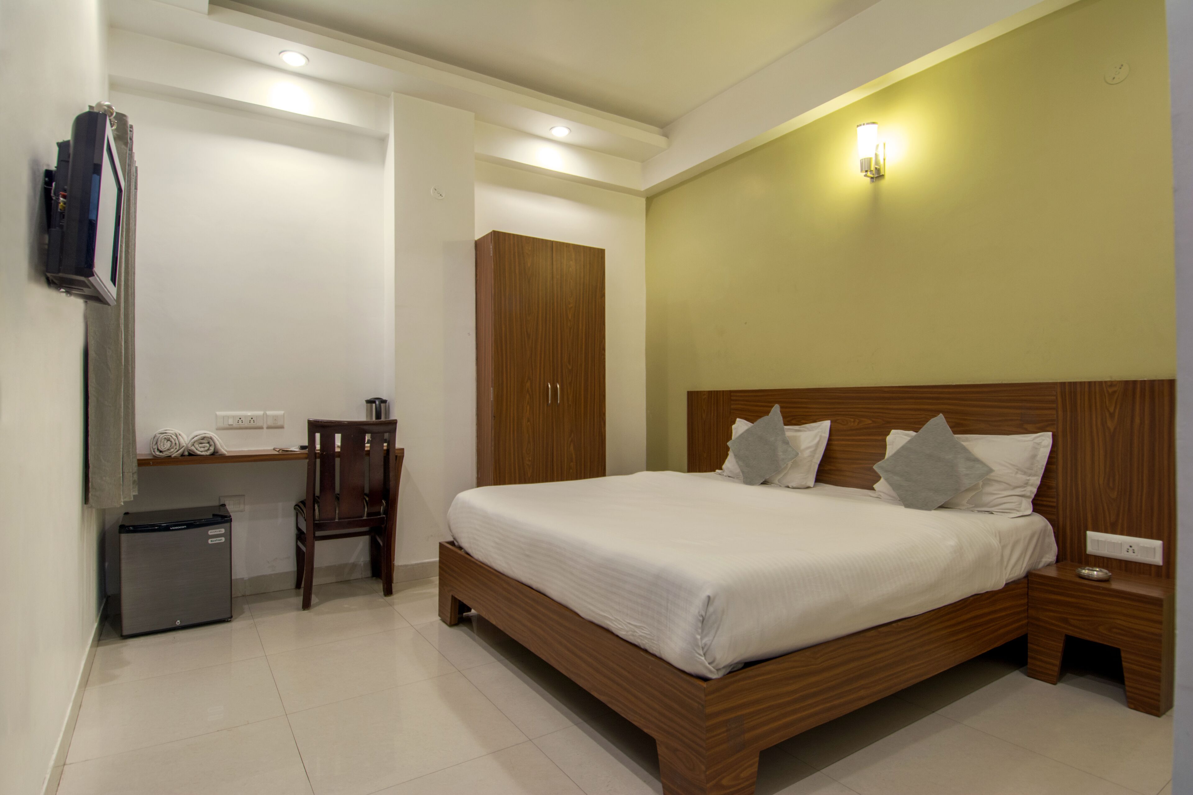 Quarto com cama de madeira, escrivaninha, cadeira e um pequeno frigorífico.