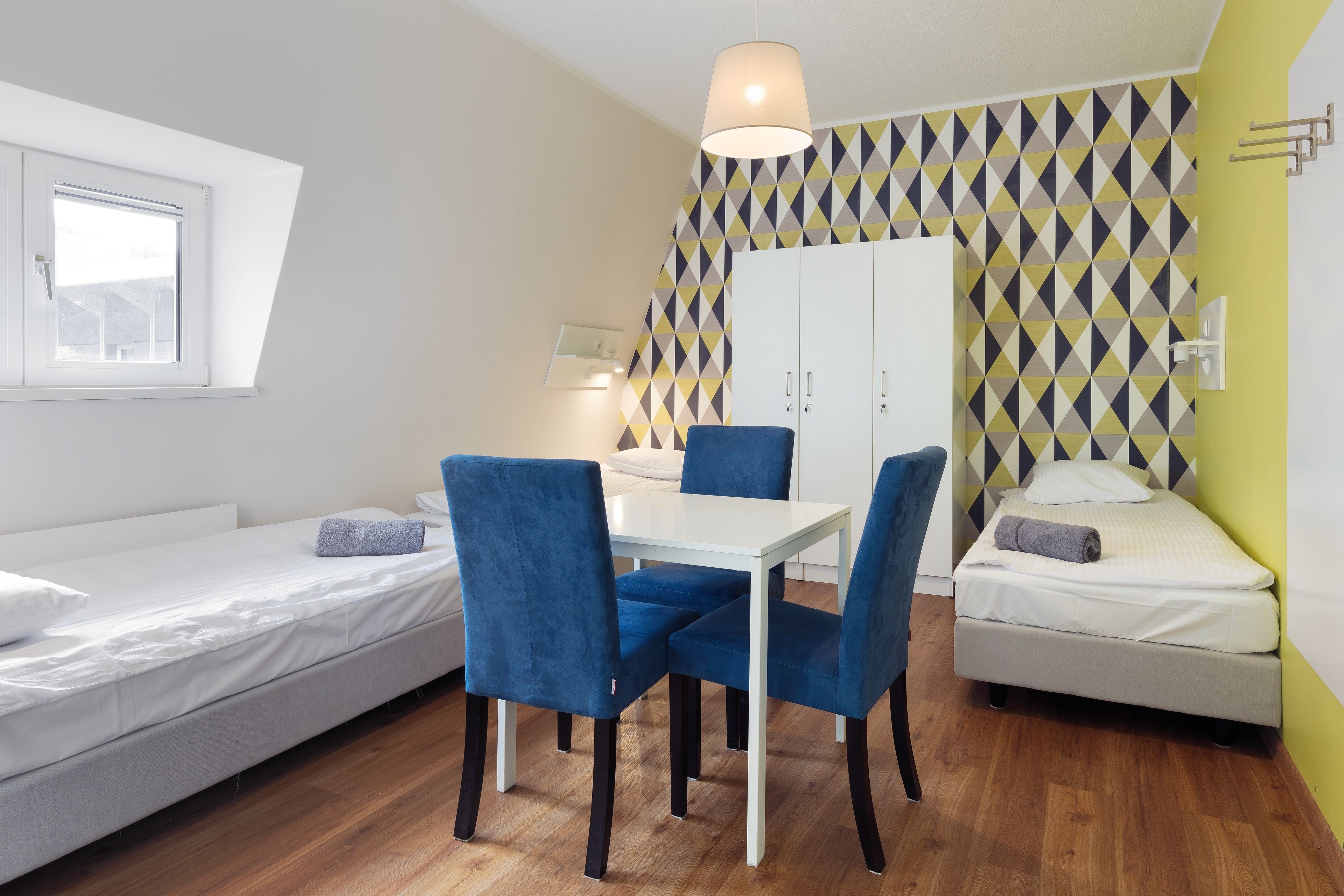Quarto compacto com cama, escrivaninha, cadeiras, armário e parede estampada.