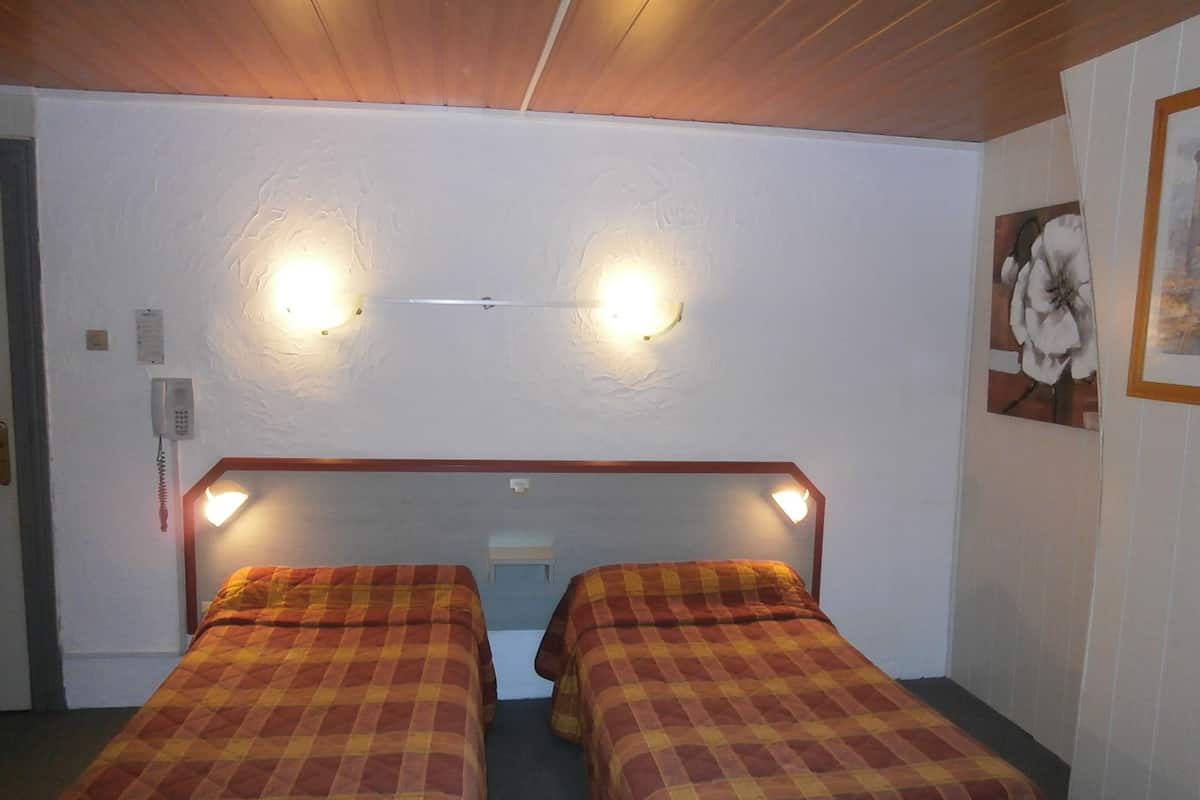 Quarto com duas camas, teto de madeira e luminária fixada na parede.