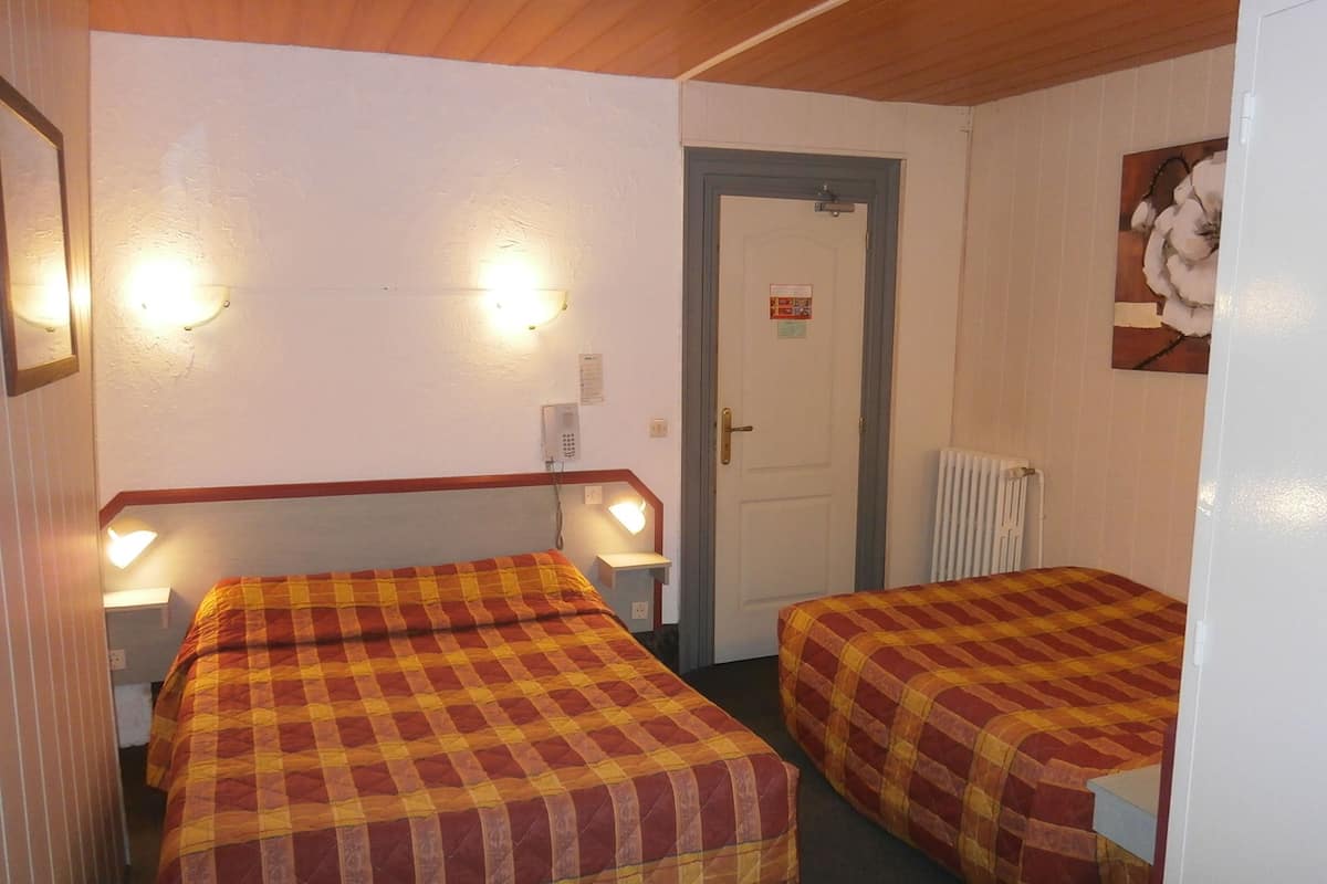 Quarto com duas camas, cada uma com colcha xadrez, luminária ao lado da cama, telefone fixado na parede e porta com uma placa.