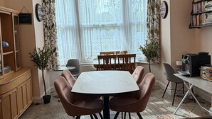 Uma sala de jantar com mesa e cadeiras, um lustre, uma estante de livros e uma janela com cortinas.