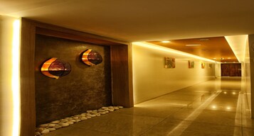 Um corredor com parede de destaque em madeira, borda de pedrinhas e uma série de obras de arte emolduradas na parede.