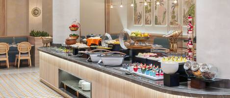 Uma área de buffet com diversos tipos de comida, um espaço de estar com cadeiras e um piso estampado.