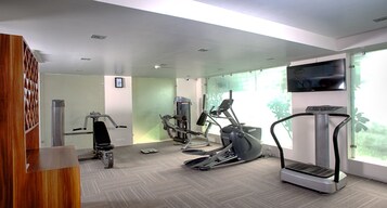 Uma academia moderna com equipamentos de cardio, um banco de musculação e uma TV na parede.