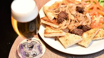 Prato de comida com pão, cebolas e carne, e um copo de cerveja sobre uma mesa.