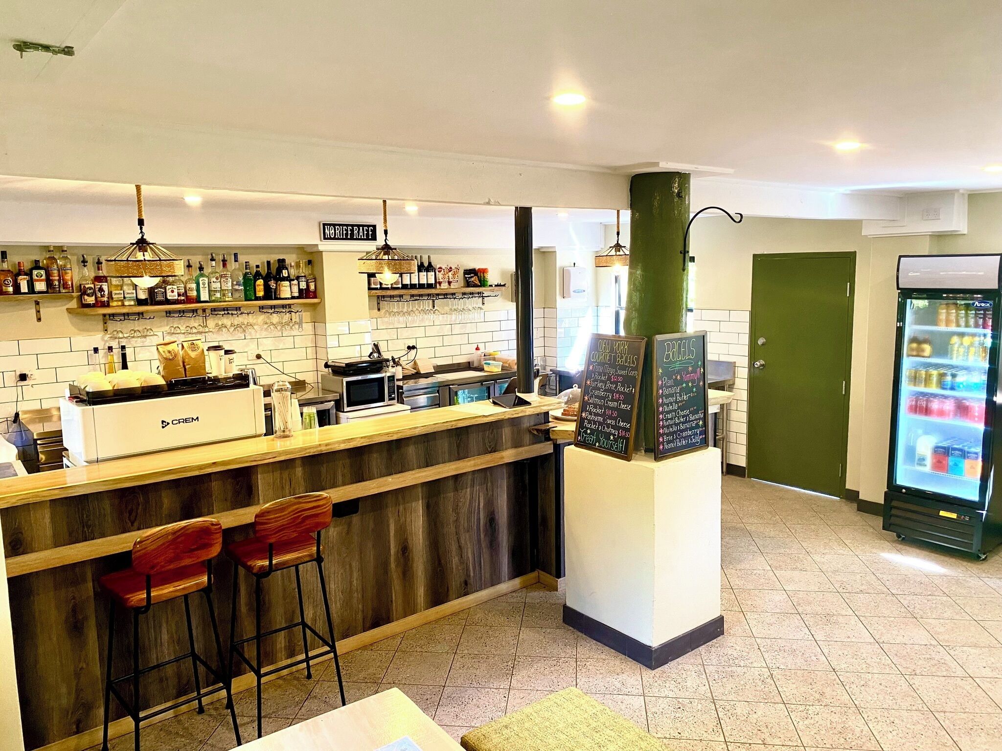 Um café com área de bar, um refrigerador com bebidas e uma placa com a inscrição 'No Riff Raff'.