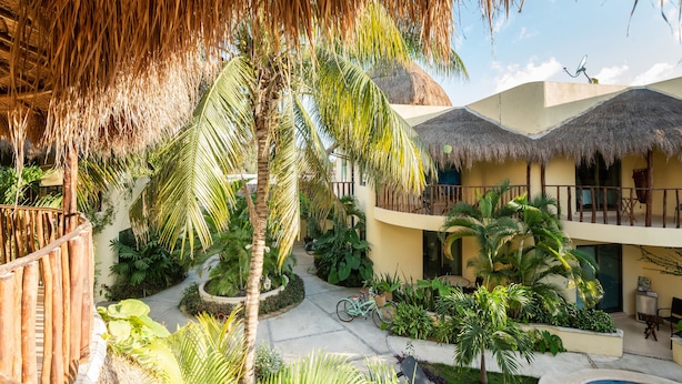 Pátio de resort com piscina, palmeiras e um edifício com telhado de palha.