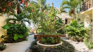 Um pátio exuberante com um jardim central, cercado por plantas tropicais e um banco de madeira.