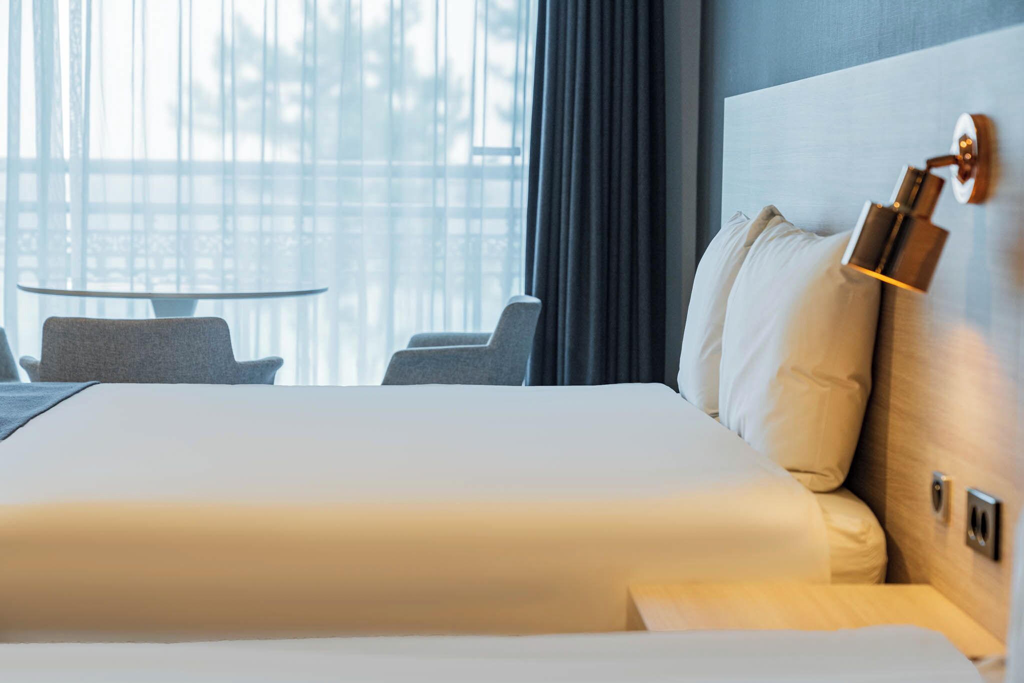 Quarto de hotel moderno com cama grande, mesa de cabeceira e uma cadeira.